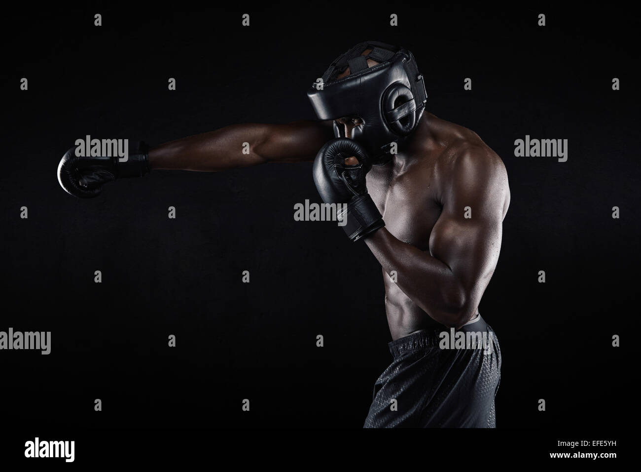 Side view of tough young male boxer practicing on black background ...