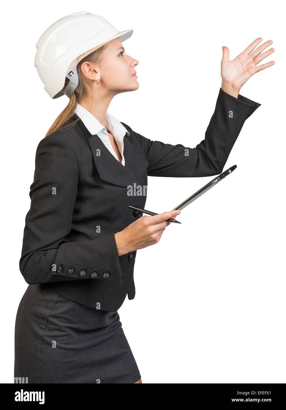 Businesswoman wearing hard hat, with clipboard and pen, pointing at ...