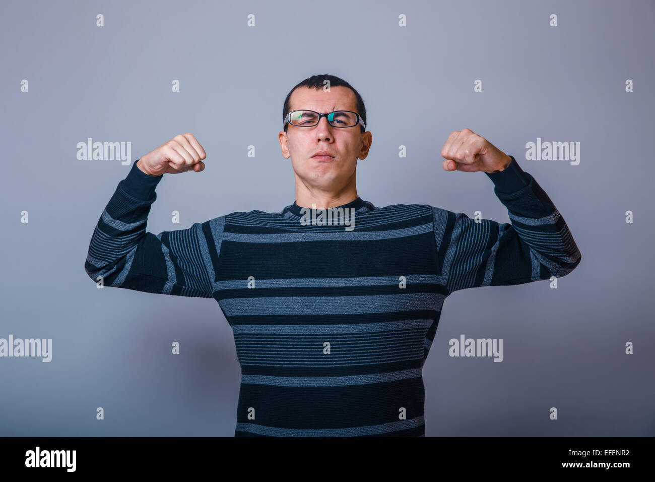male of European appearance brunet showing strength on a gray ba Stock ...