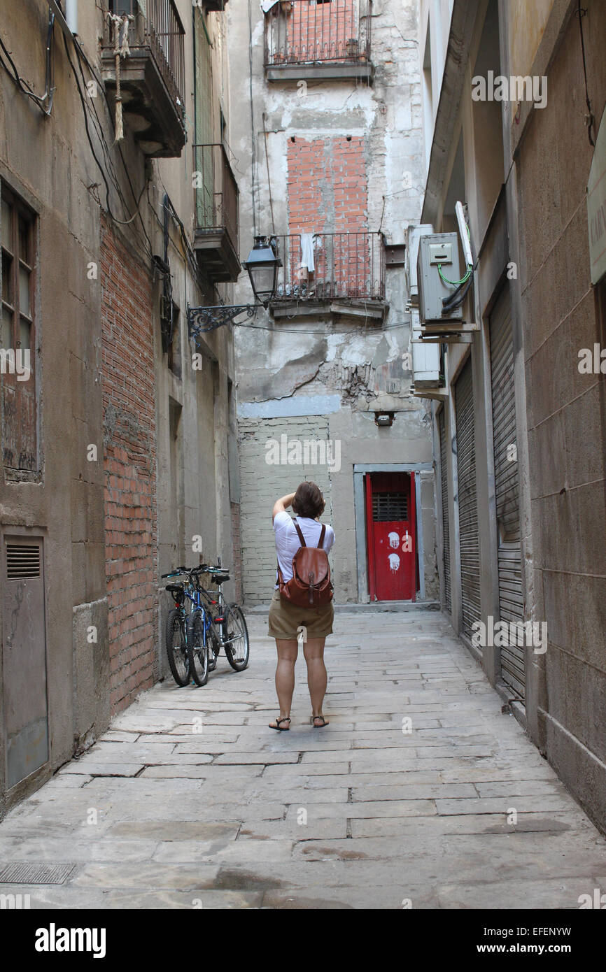 Woman taking photos in narrow back street with bricked up doors and ...