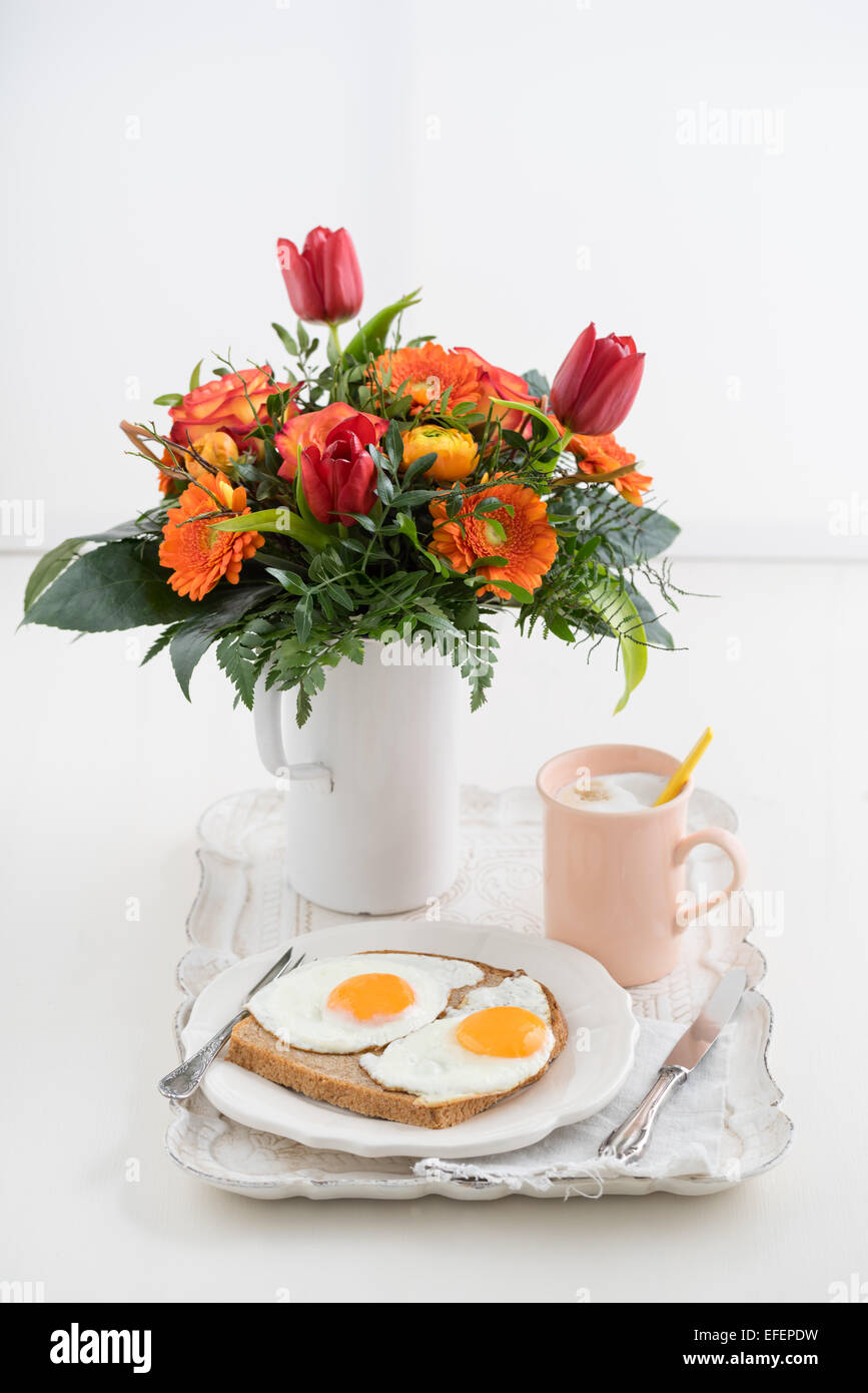 Breakfast with fried eggs, cappuccino and a bouquet of flowers on a ...