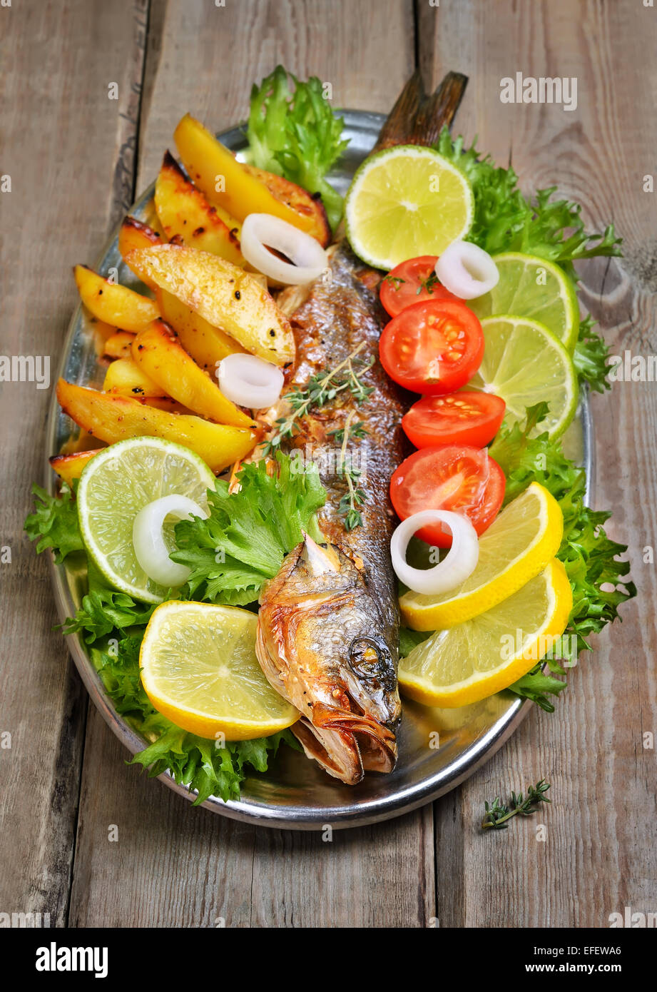 Grilled fish with fresh vegetables and baked potato wedges on wooden ...