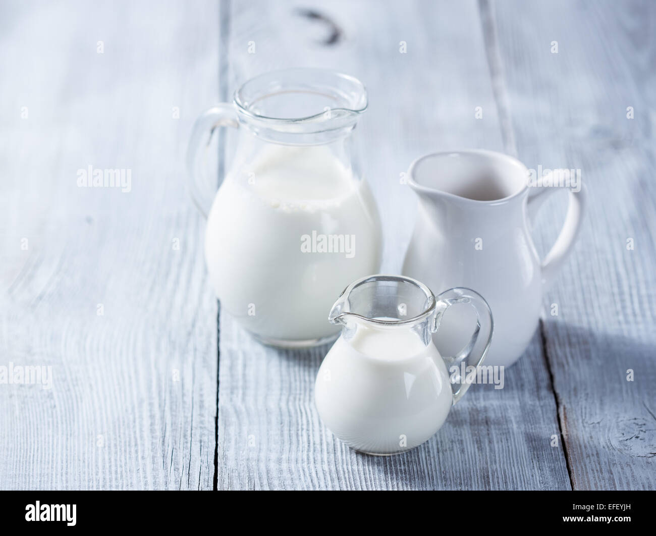 Three milk jars on white wooden background Stock Photo - Alamy