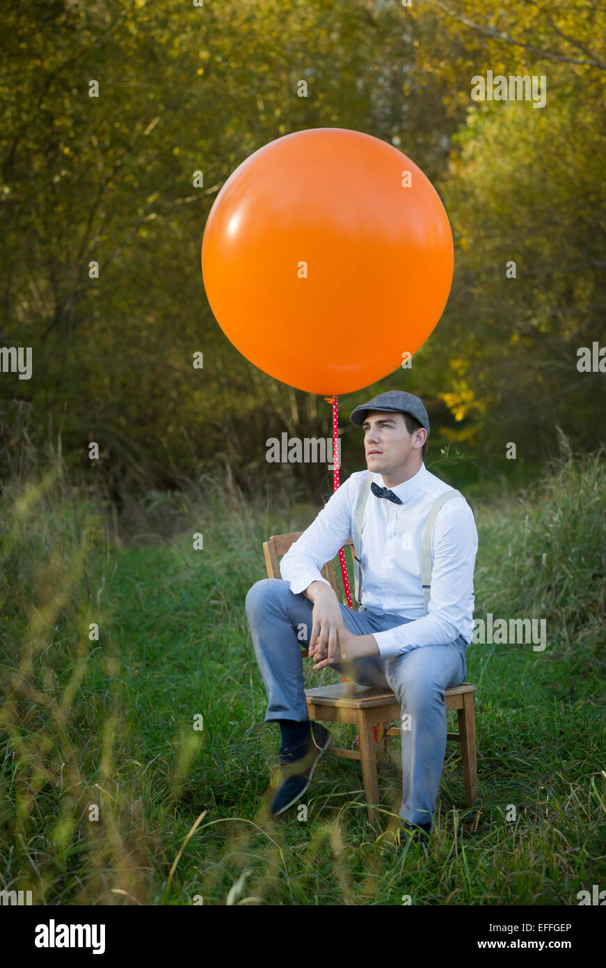 Man sitting on chair with balloon on meadow Stock Photo - Alamy