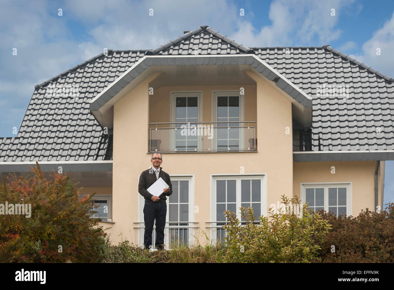 Estate agent with documents standing in front of residential house ...