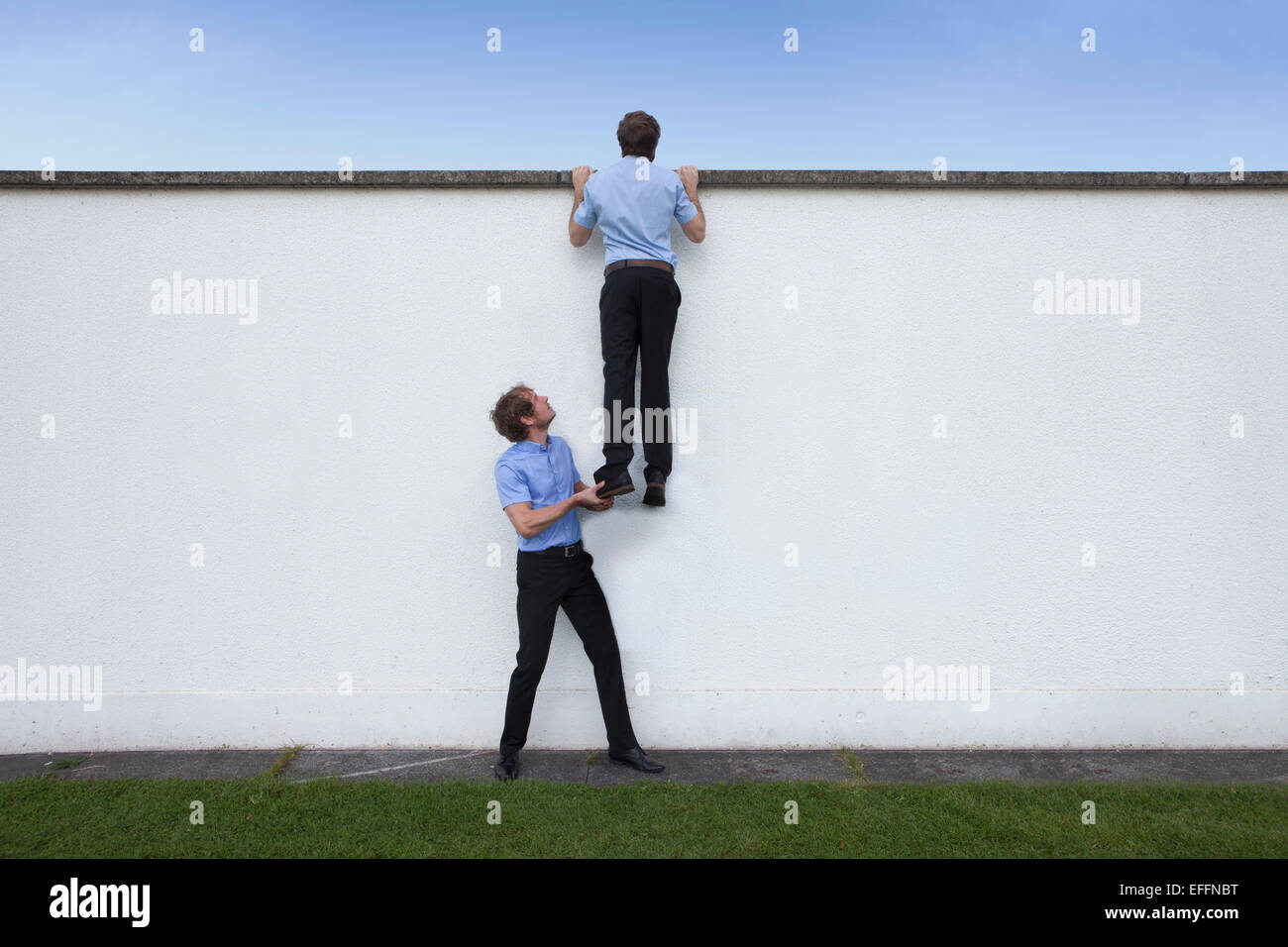 Business man helping colleague on wall Stock Photo - Alamy