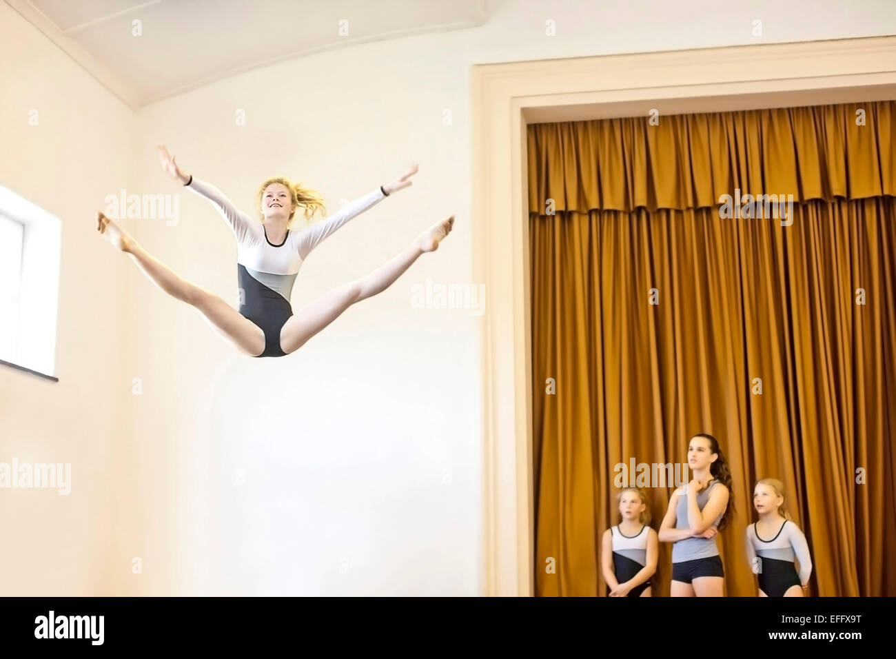 Girl in gymnastics outfit doing aerial jump with three girls watching ...
