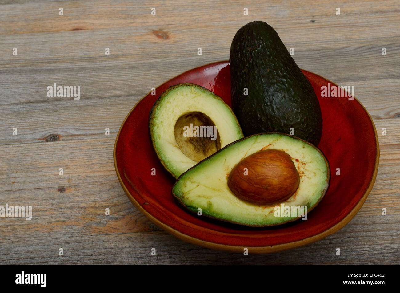 whole avocado and two halves on a red ceramic bowl Stock Photo - Alamy