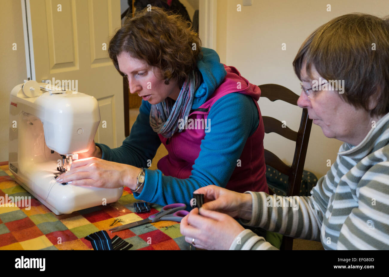 Daughter operating sewing machine, with mother assisting Stock Photo ...