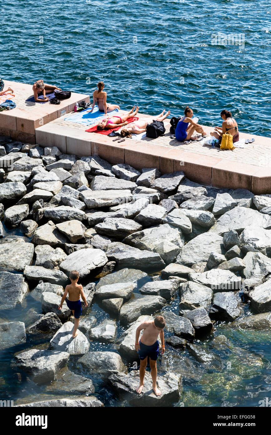 Young people sunbathing and looking out over water, Tjuvholmen, Oslo ...