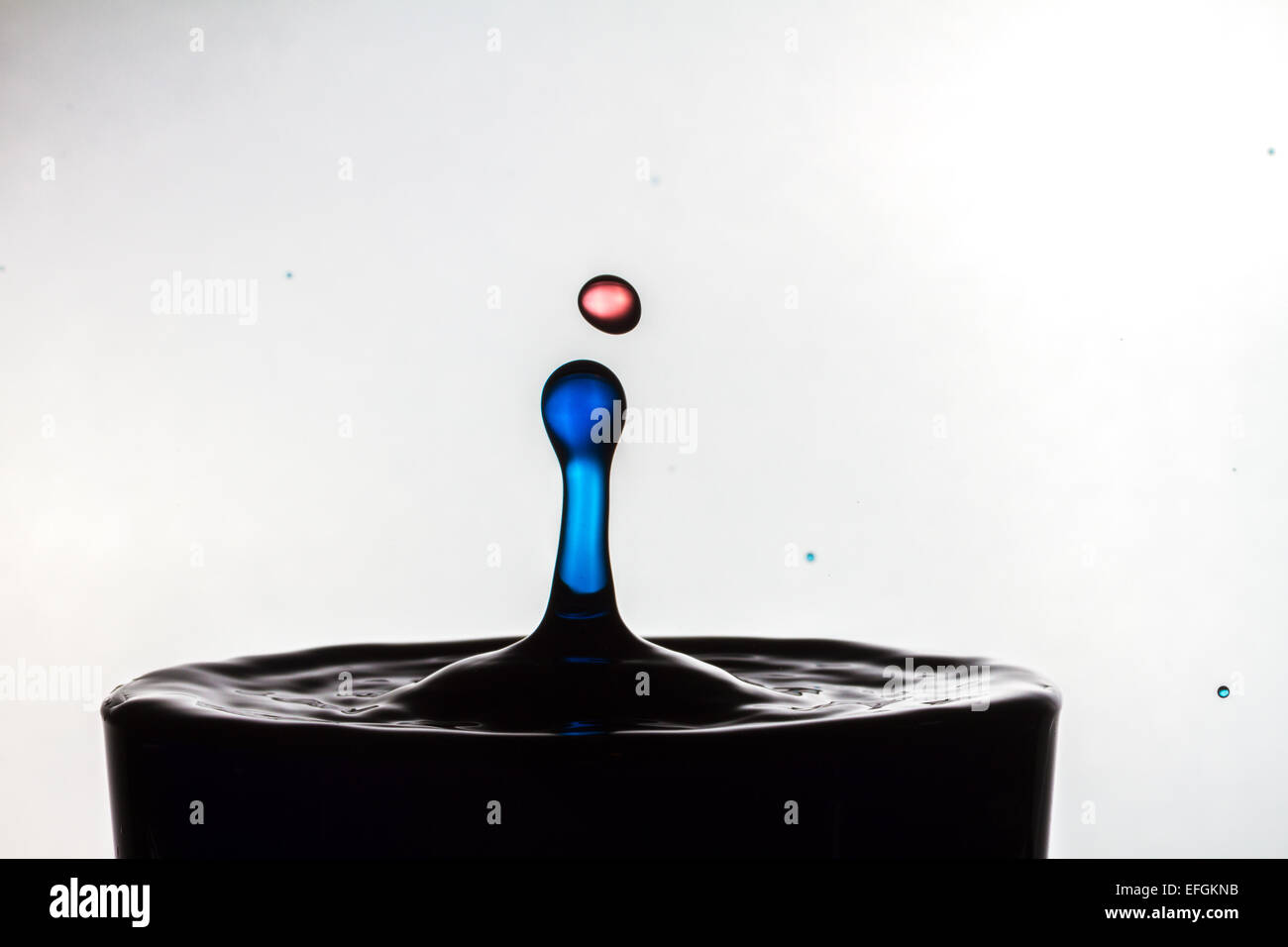 A red water droplet about to hit a blue splash of water. Splashes of ...