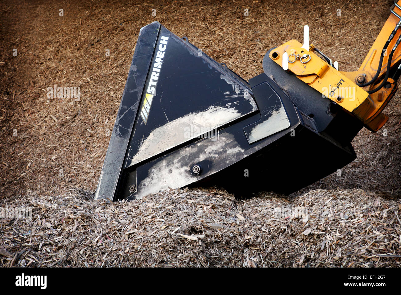 Digger moving forestry waste from loading bay at biomass plant Stock ...
