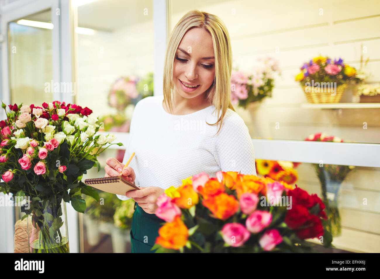 Young florist making notes in notepad during working day in the shop ...