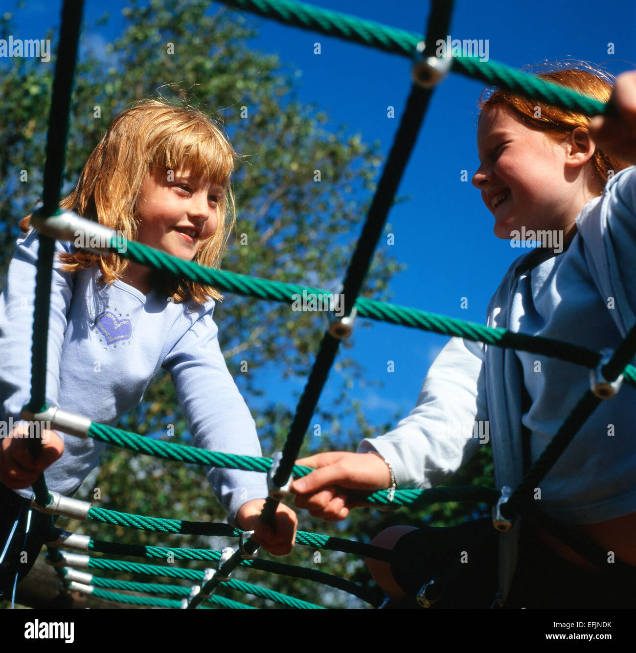Two girls having fun playing on climbing frame in sunshine in the park ...