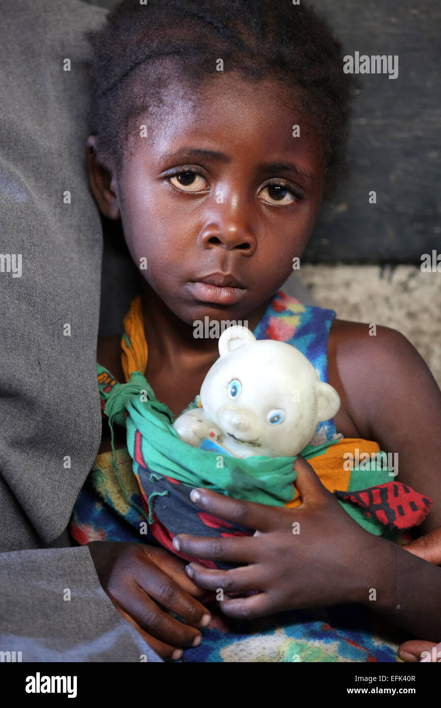 Fearful looking orphan girl (5 years) with her toy in the arms of a ...