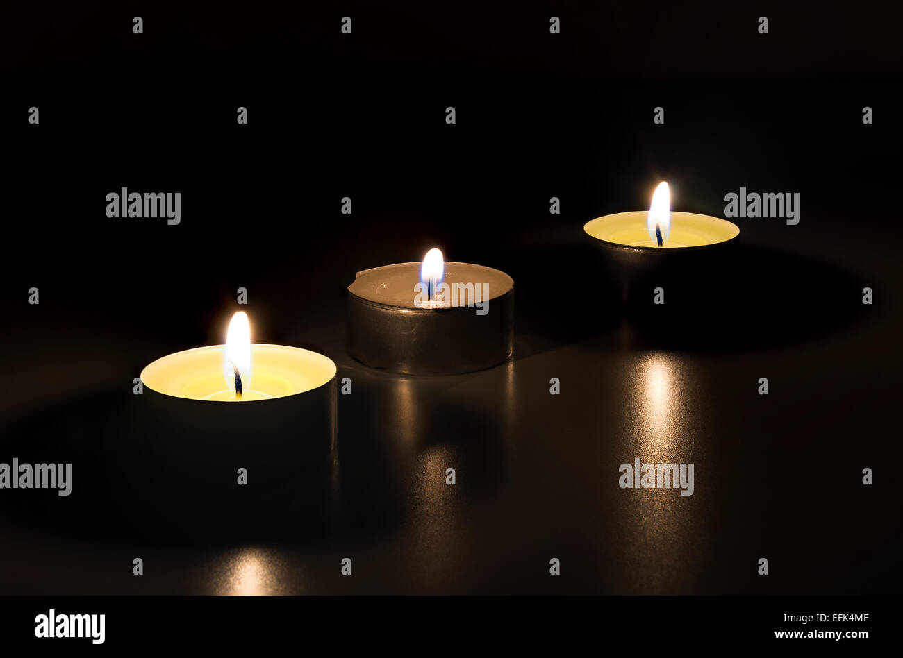 Three yellow burning candles in the dark Stock Photo - Alamy