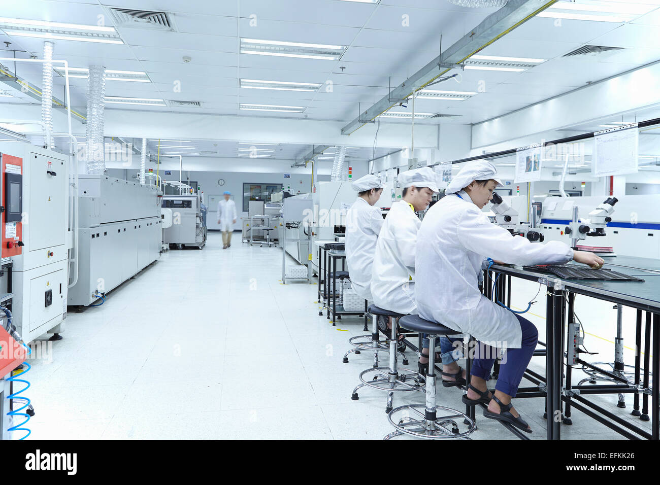 Workers using microscopes in factory that specialises in creating ...