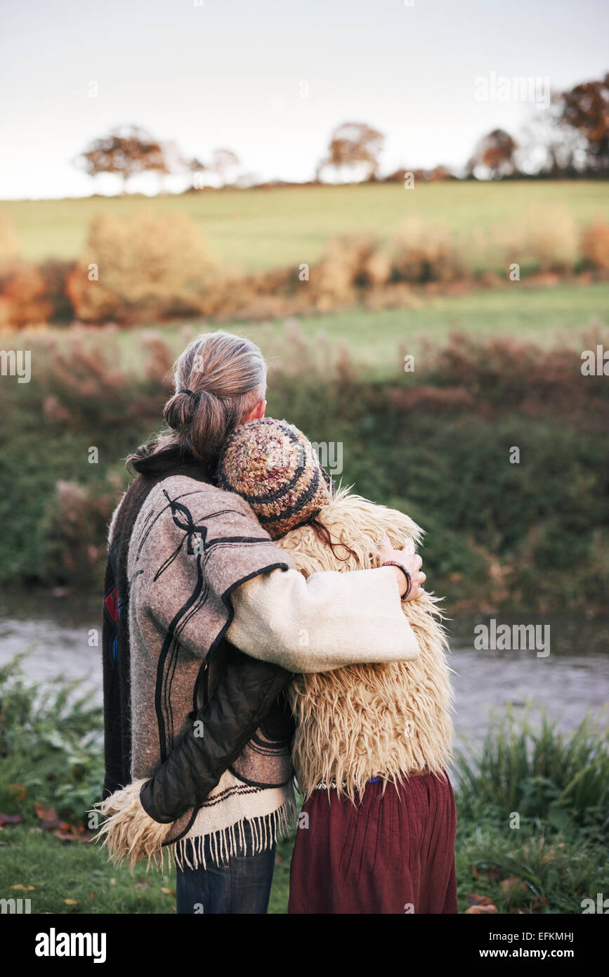 Rear view of mature hippy couple watching sunset at riverside Stock ...