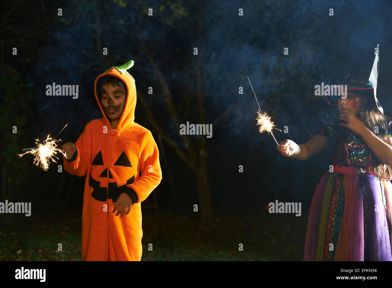 Brother and sister wearing halloween costumes holding sparklers in ...