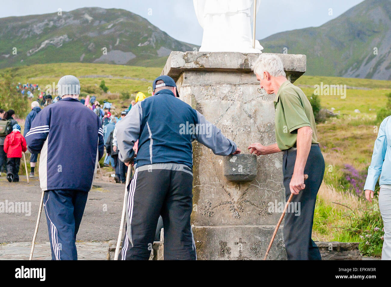 Pilgrims dip their fingers into a holy water font before climbing ...