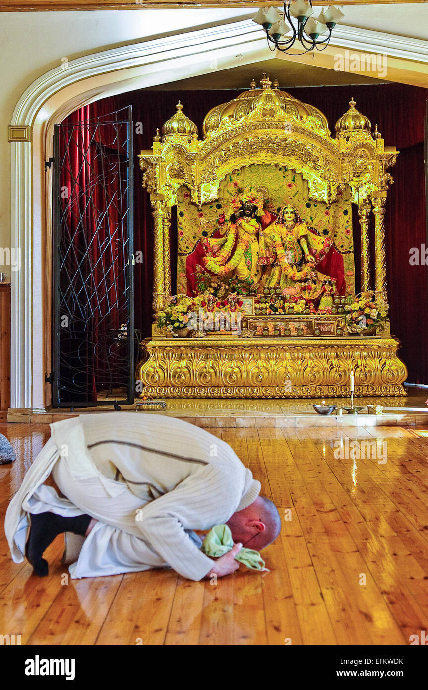 A Hare Krishna devotee wearing white robes kneels and bows his head to ...