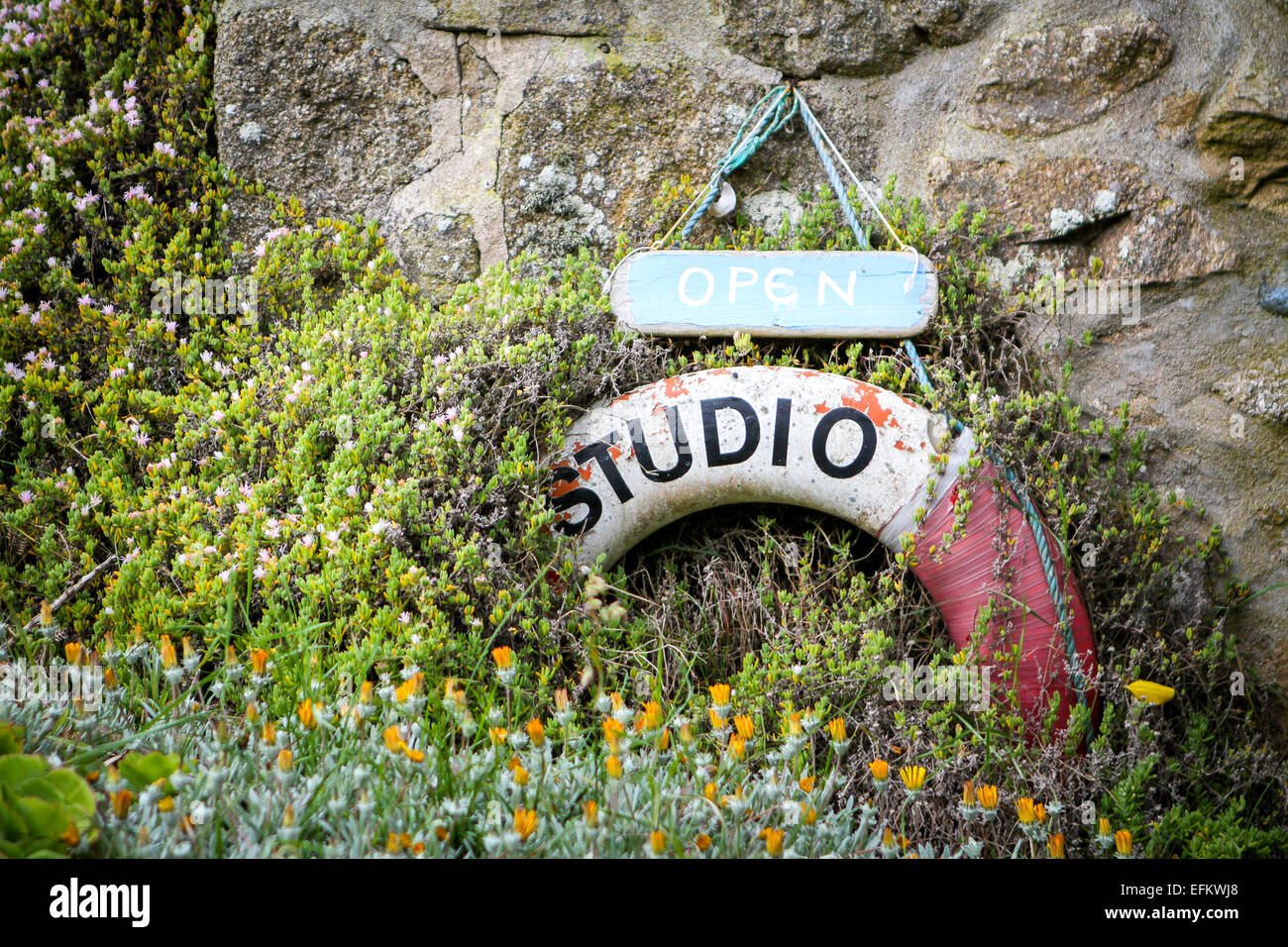 Handmade lifebuoy artist studio sign hanging on stone wall in overgrown ...