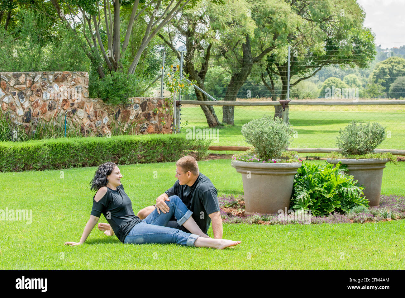 A young adult couple sitting outside their home on the lawn, talking to ...