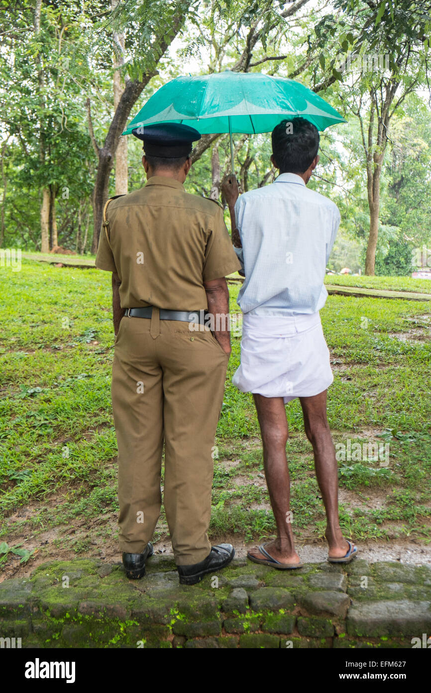 Police officer shelters under locals umbrella during heavy rainfall ...
