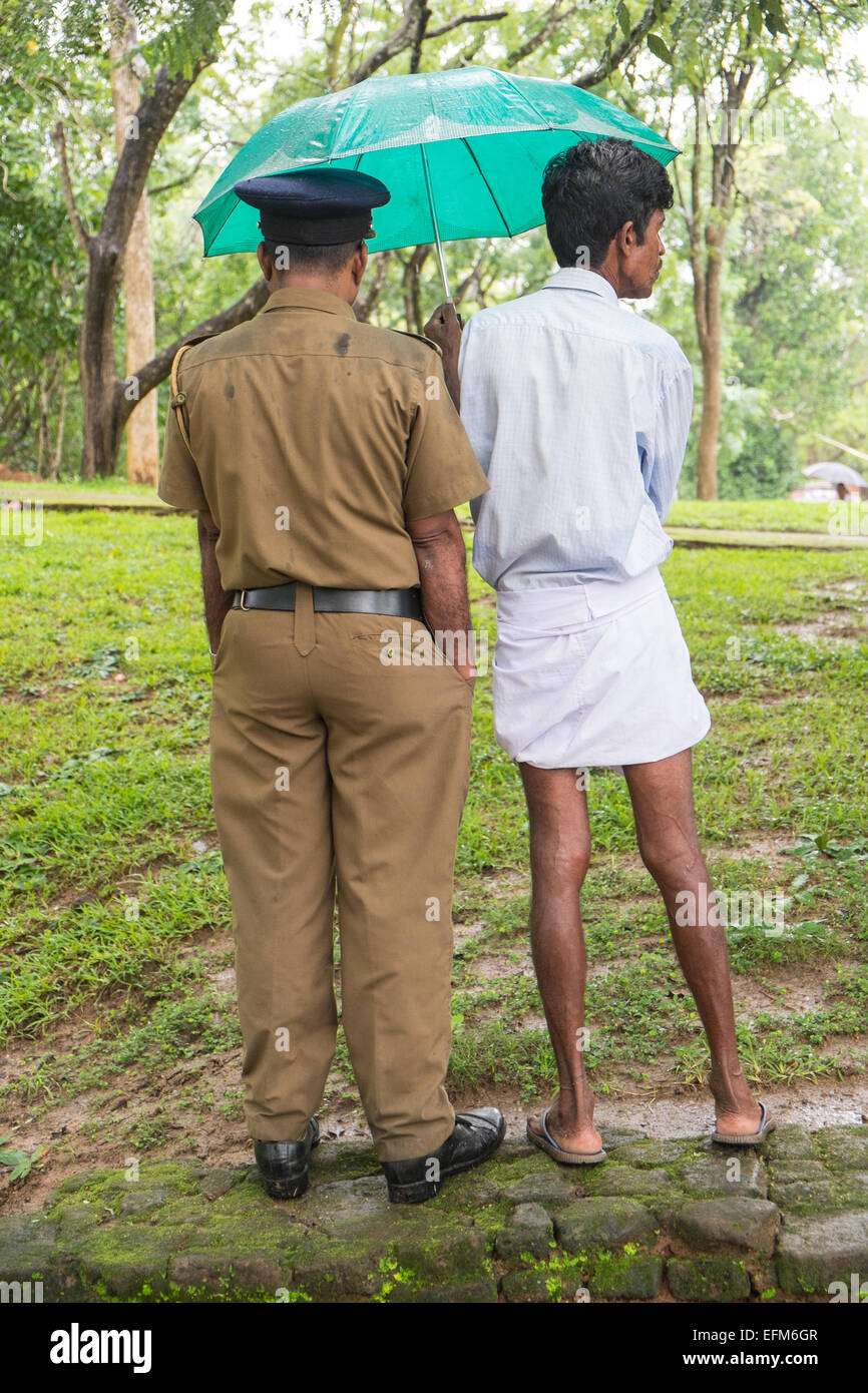 Police officer shelters under locals umbrella during heavy rainfall ...