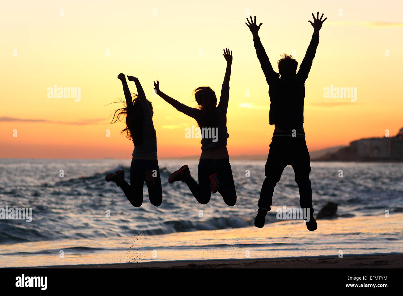 Three friends silhouettes jumping happy and raising arms on the beach ...