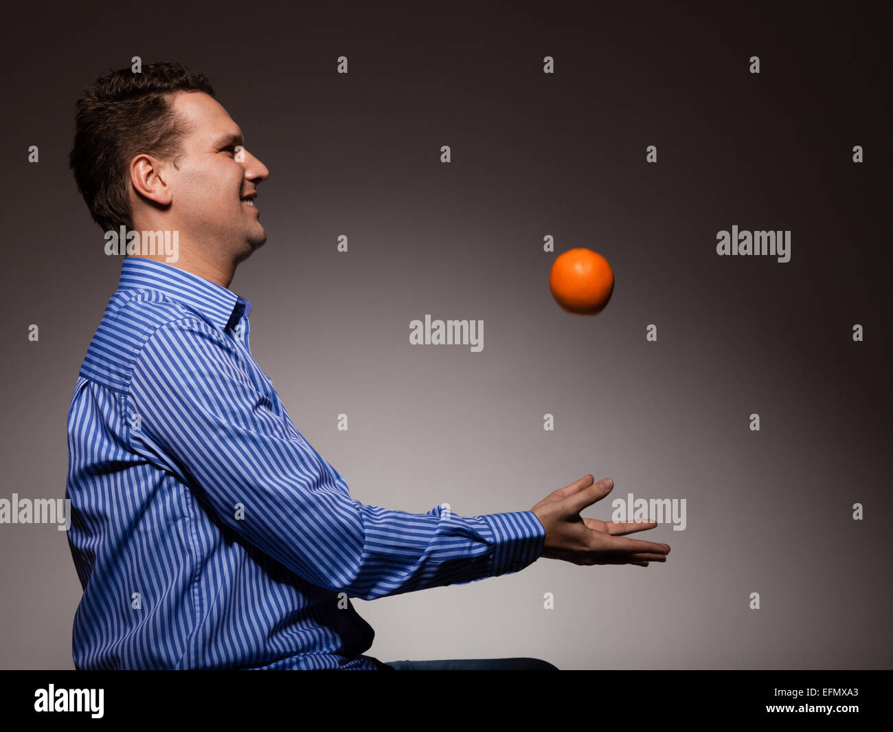 Diet and nutrition. Young smiling man throwing orange tropical fruit on ...