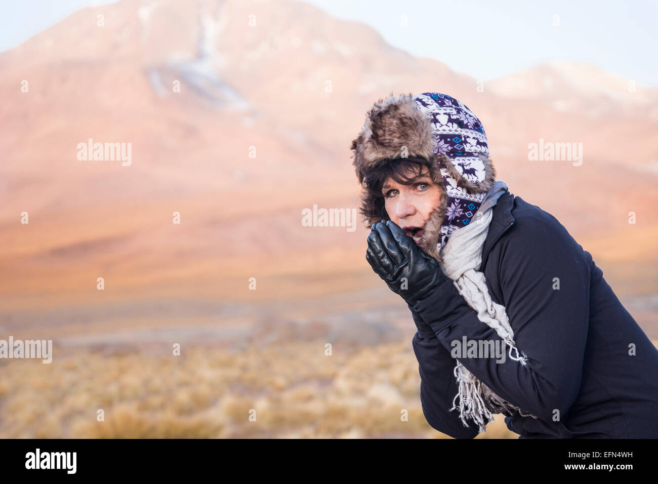Shivering woman in winter clothes tries to warm up her hands at high ...