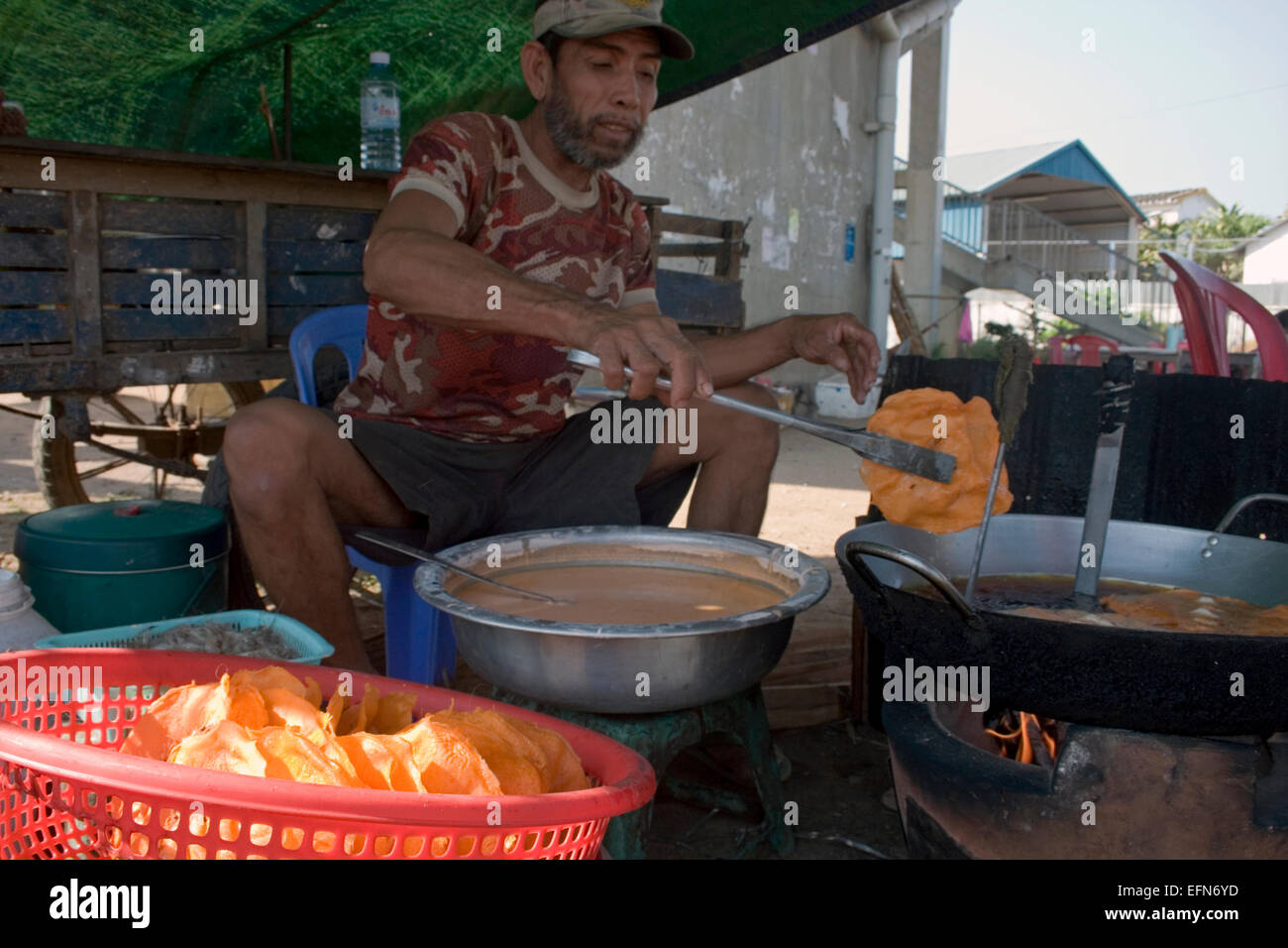 A man is cooking crunchy street food on a city street under a bridge in ...
