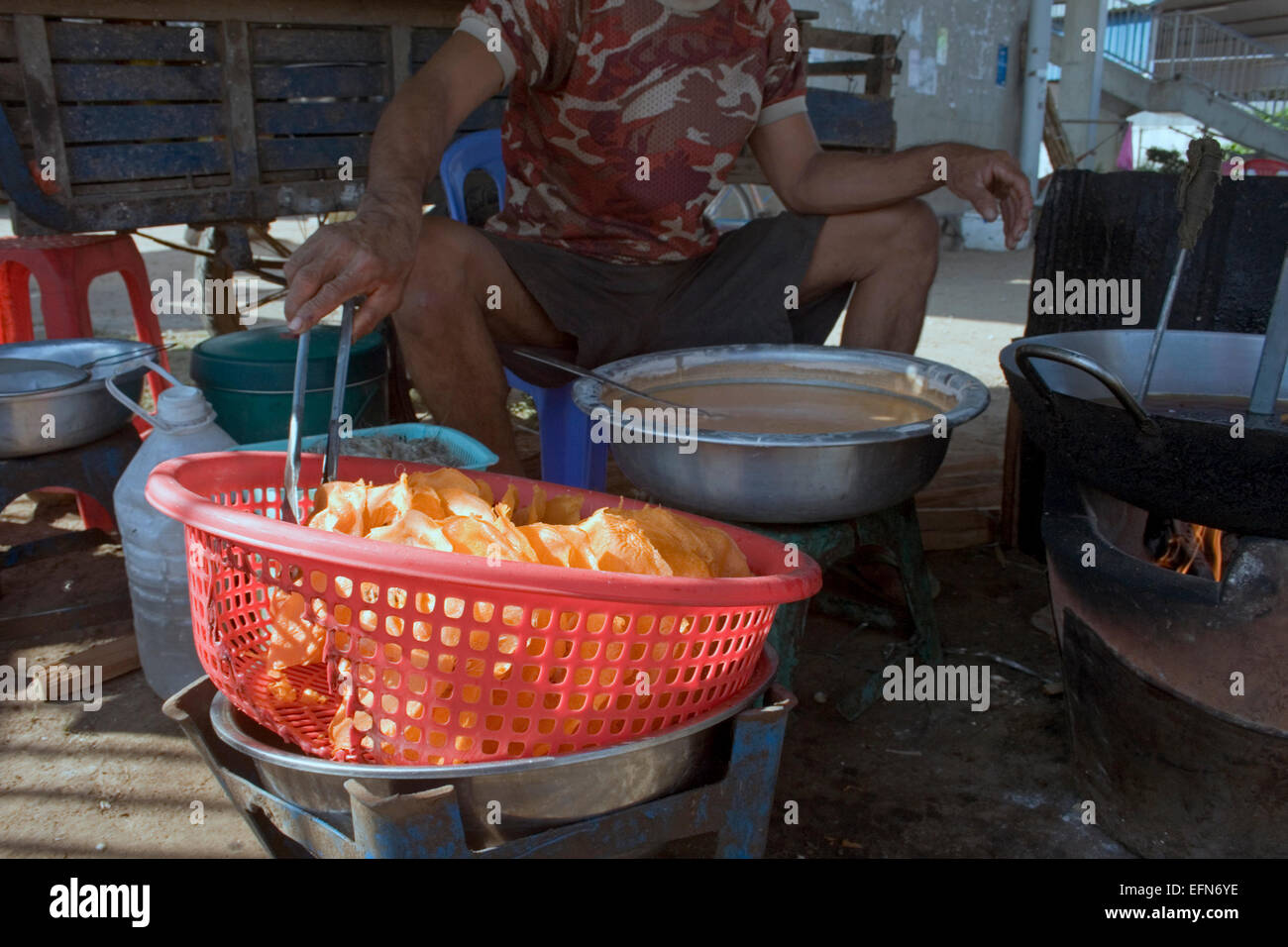 A man is cooking crunchy street food on a city street under a bridge in ...