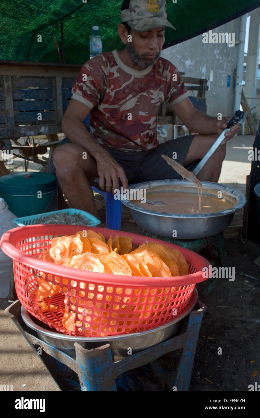 A man is cooking crunchy street food on a city street under a bridge in ...