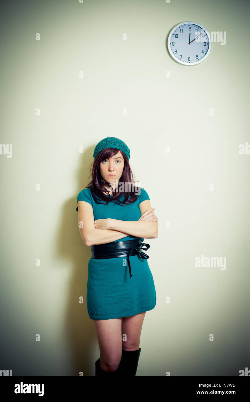 Young woman in green dress waiting under a wall clock vintage color ...
