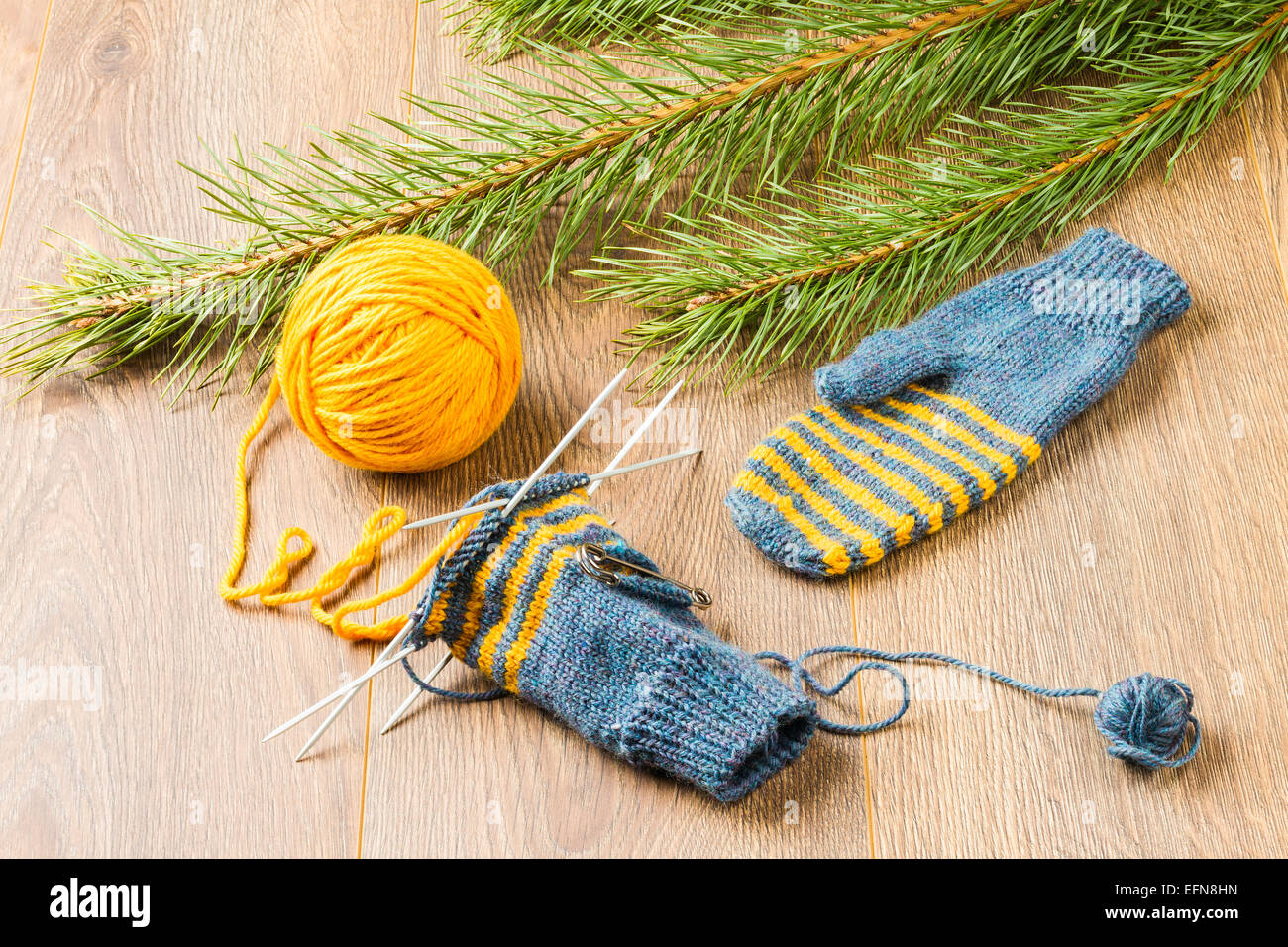 ball of threads, knitting needles, mittens and branch of pine on wooden ...