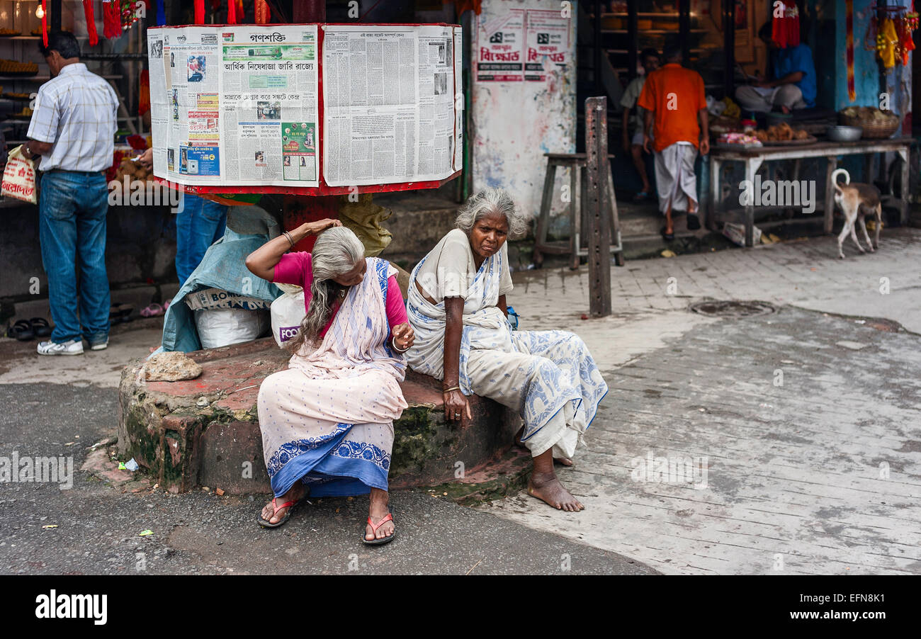 Two poor women sit under free newspaper stand in front of shops on ...