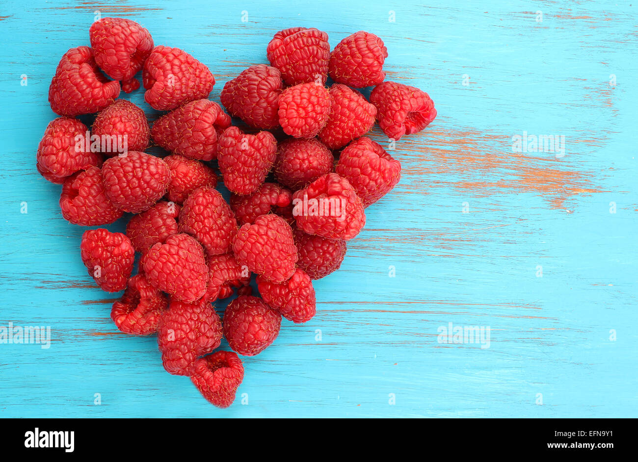 red raspberries in a heart shape on blue wooden background Stock Photo ...