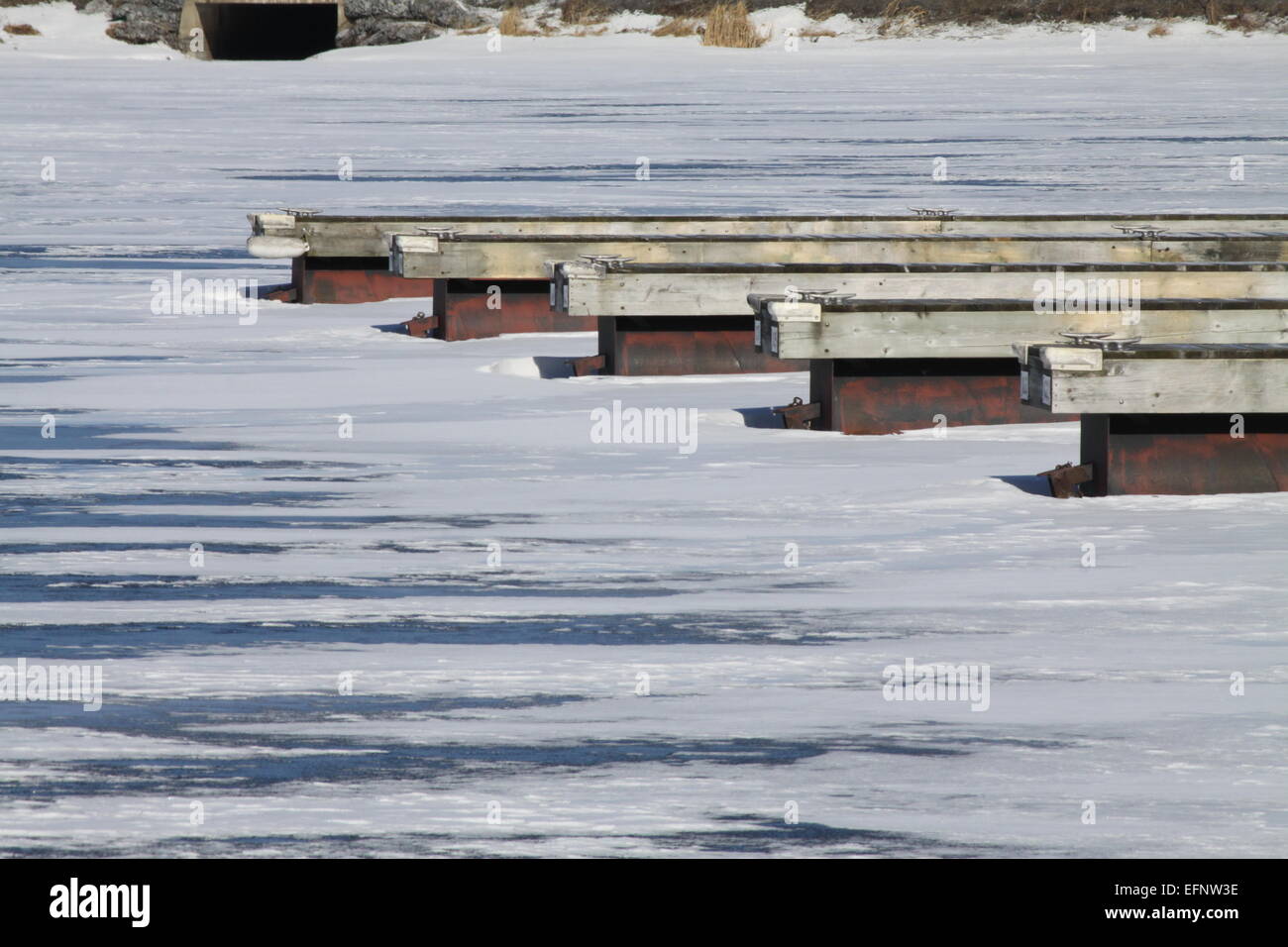 Ice & snow covered marina, wooden boat dock vacant of boats, during the ...