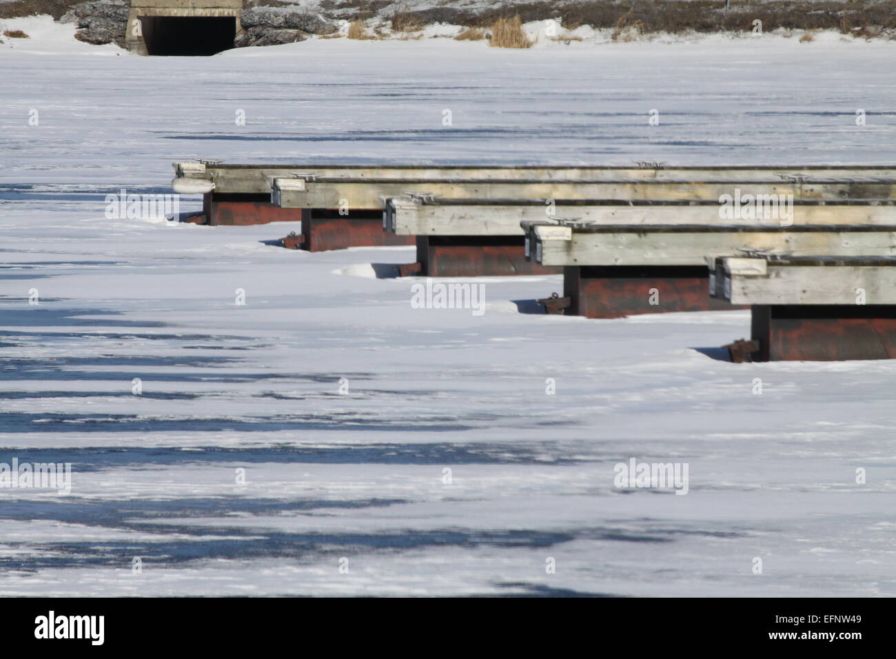 Ice & snow covered marina, wooden boat dock vacant of boats, during the ...