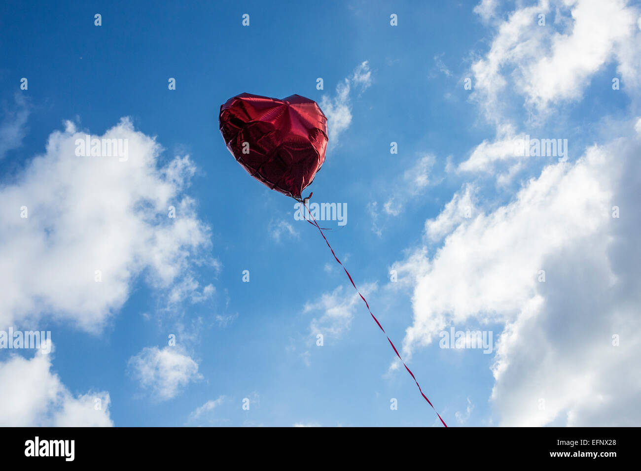 A red heart shaped helium balloon in a blue cloudy sky Stock Photo - Alamy