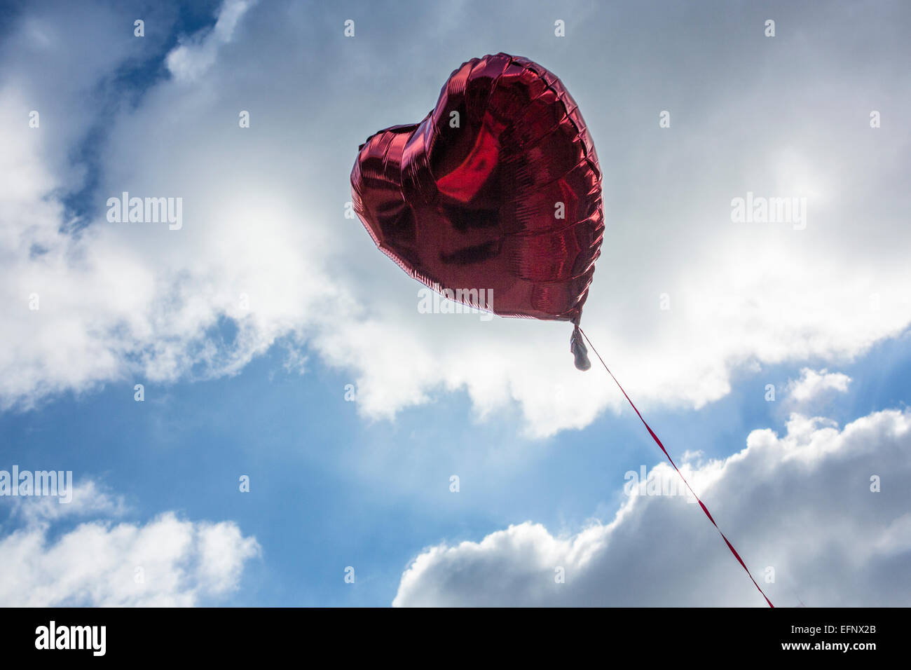 A red heart shaped helium balloon in a blue cloudy sky Stock Photo - Alamy