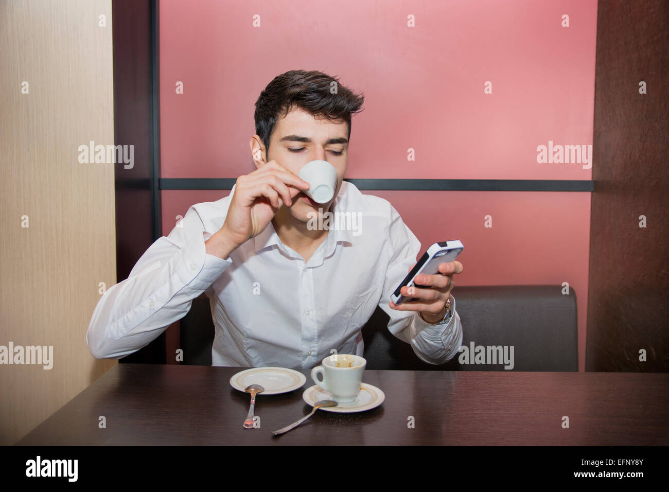 Young Man Drinking Coffee While Looking at Phone Stock Photo - Alamy