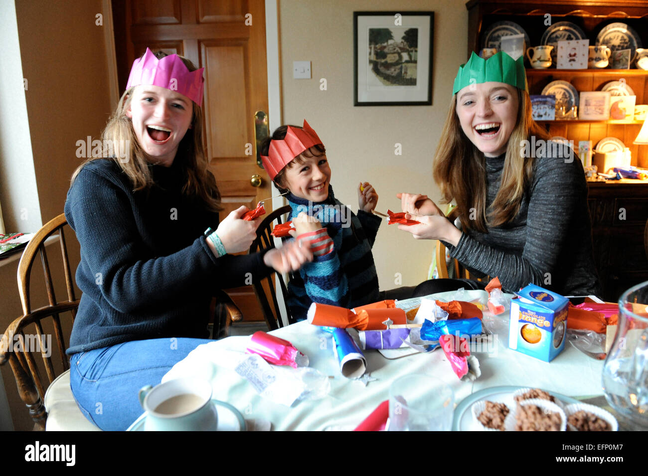 Three young cousins pulling crackers at the Christmas dinner table ...