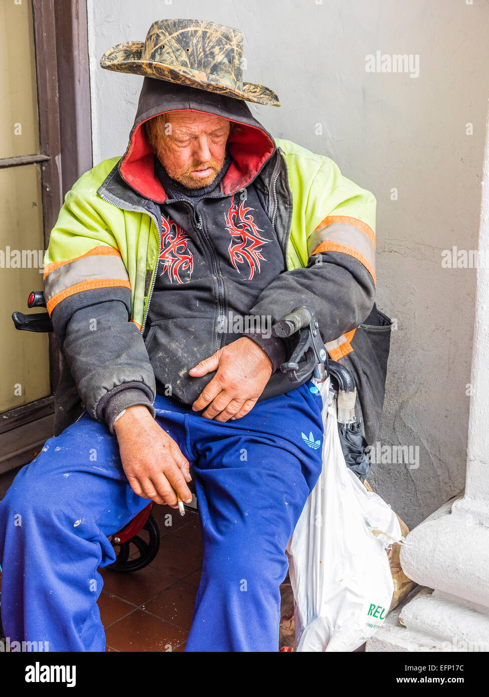 A homeless man smokes a cigarette in an enclosure outside in the front ...