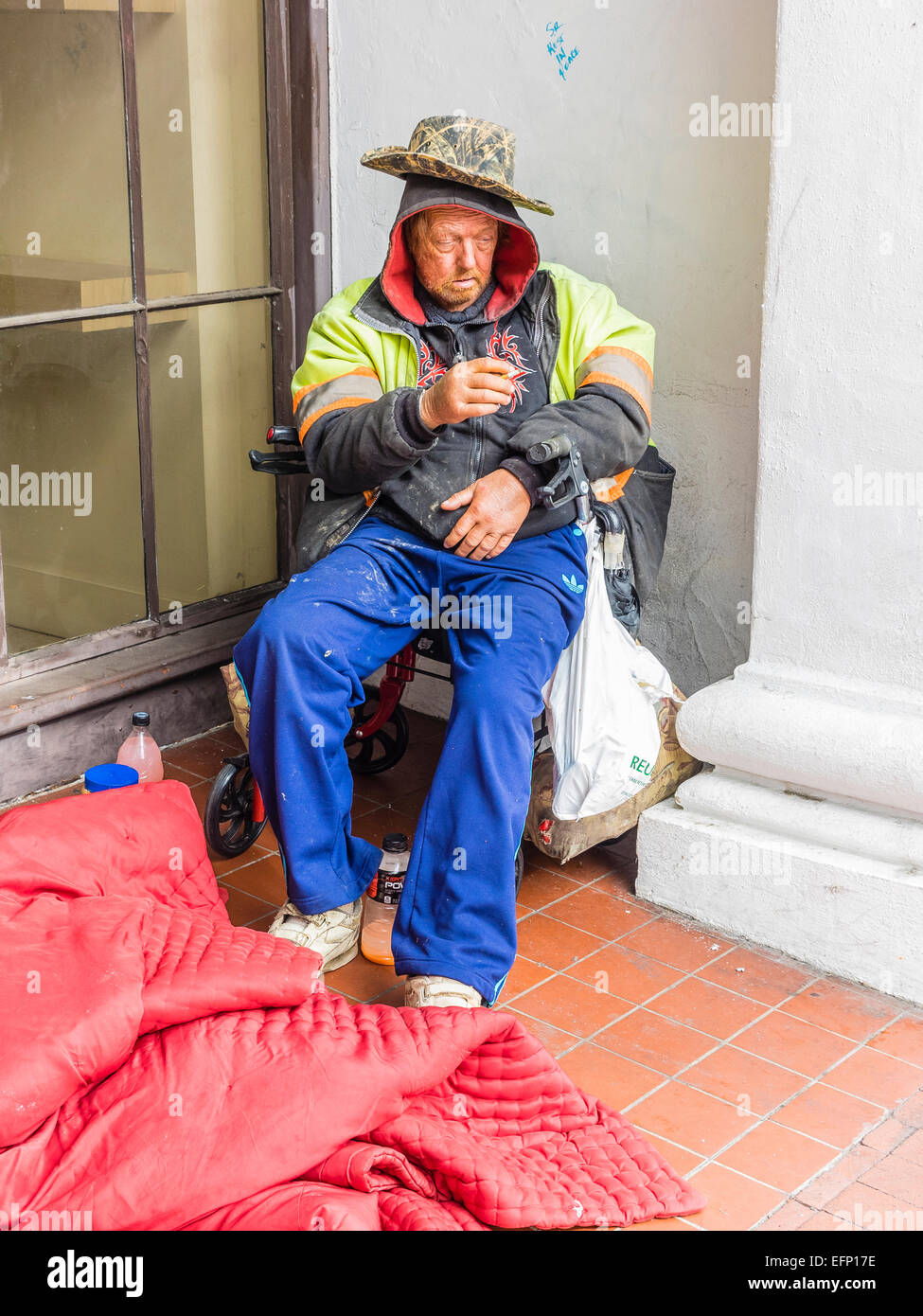 A homeless man smokes a cigarette in an enclosure outside in the front ...