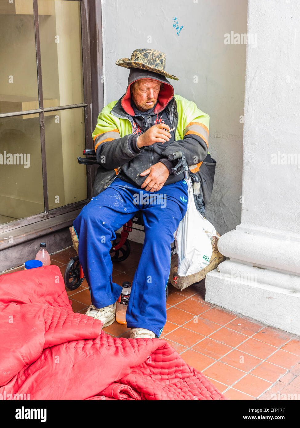 A homeless man smokes a cigarette in an enclosure outside in the front ...
