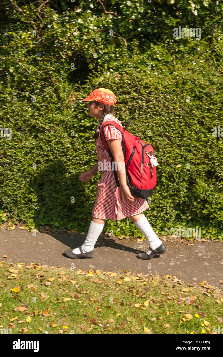 Young girl in red primary school uniform walking along footpath beside ...
