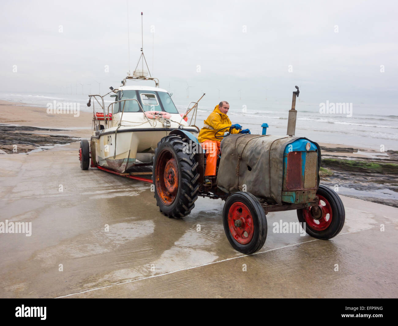 Fisherman driving a tractor hauling his boat up the slipway from the ...